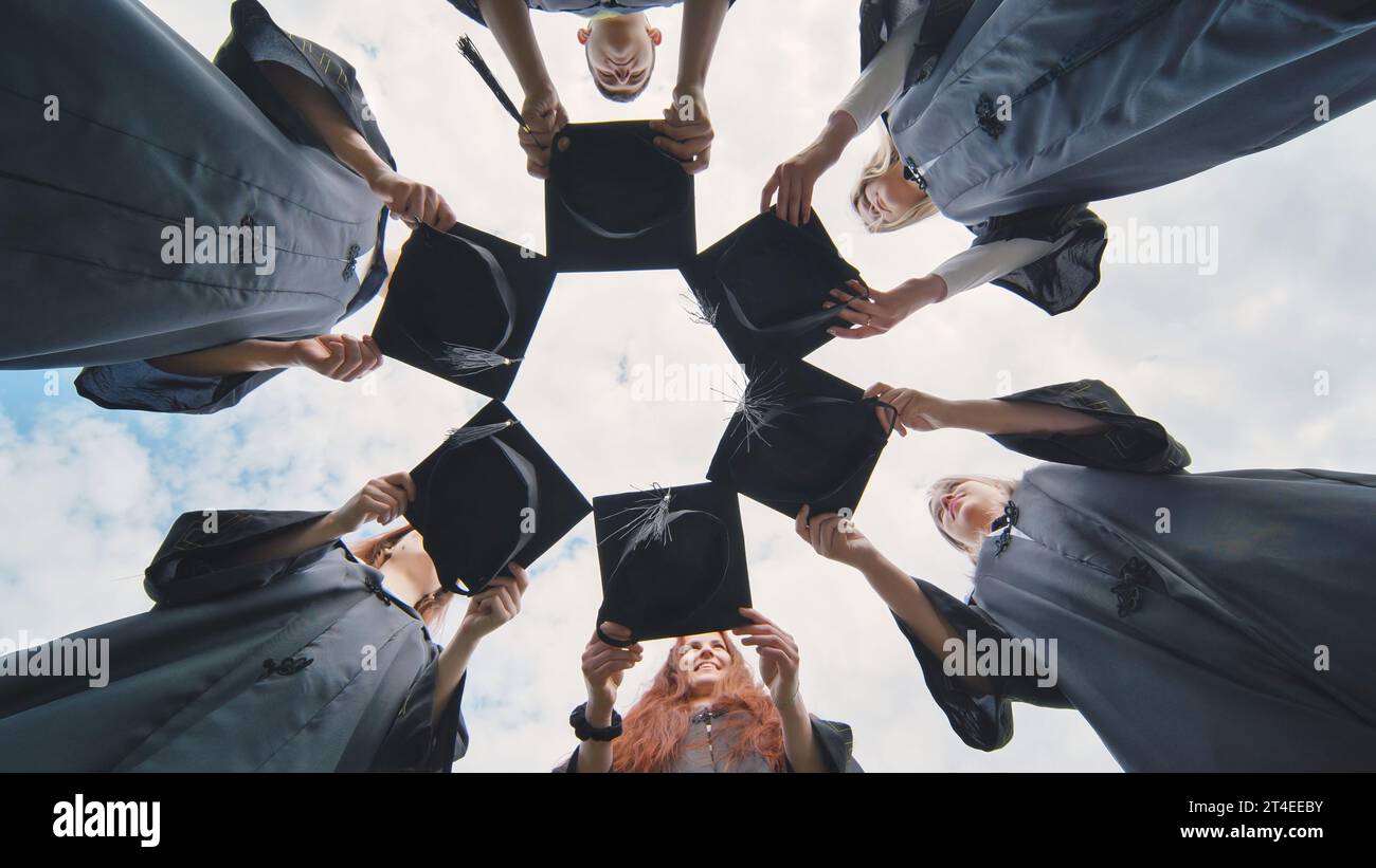 Graduates in black robes join their caps in a circle Stock Photo - Alamy