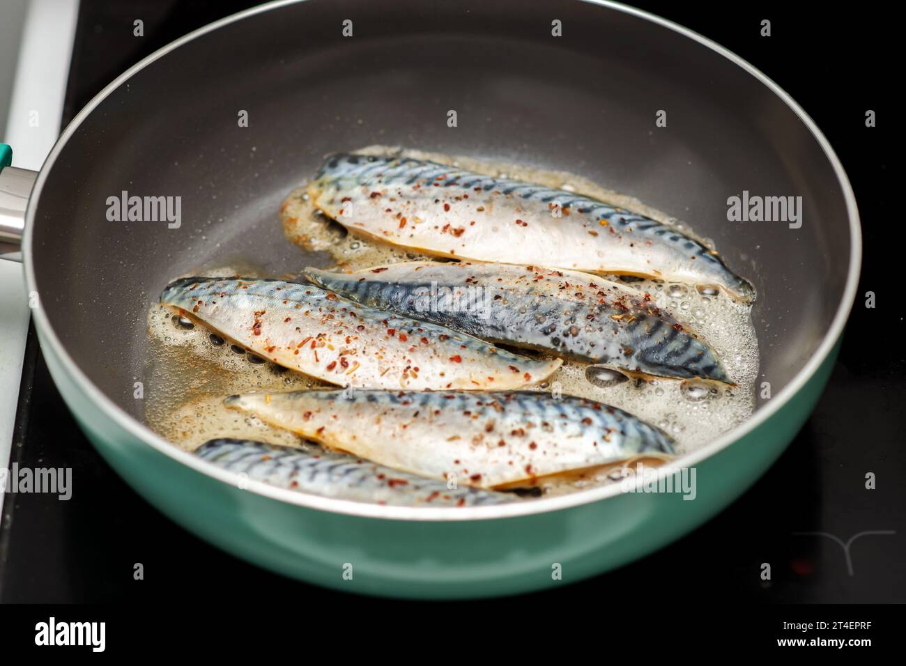Raw fish fillet sprinkled with salt and spices is fried in a frying pan ...
