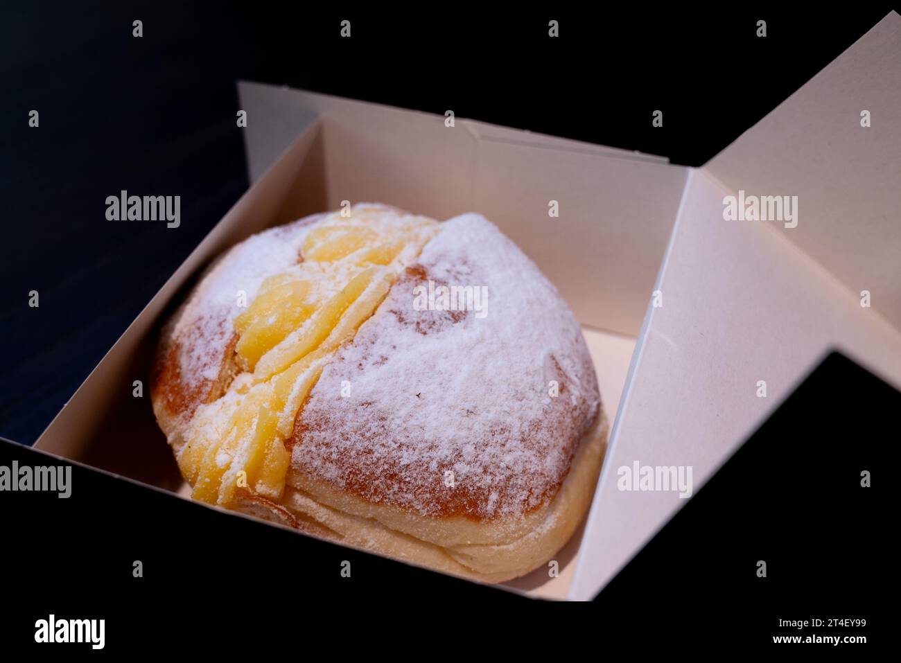 sugar coated doughnut with custard served in cardboard box to take away ...
