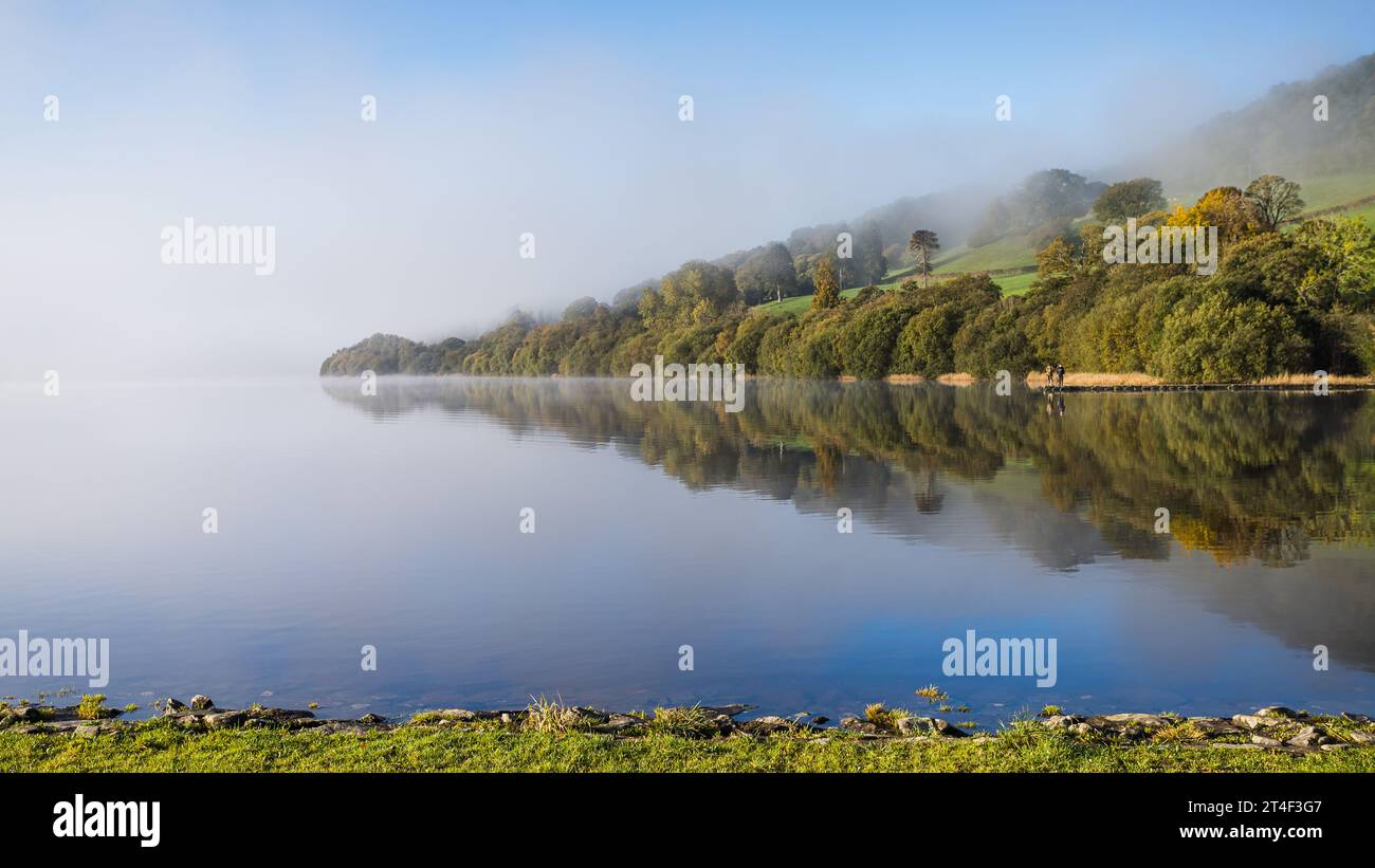 Reflections of trees and two men fishing on Lake Bala as the morning ...