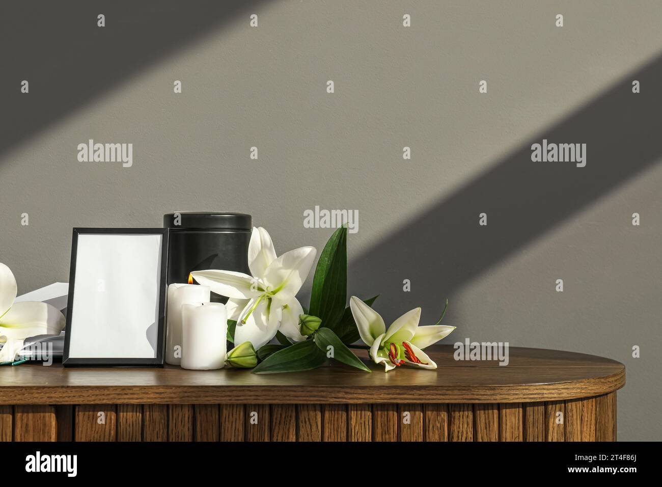Blank funeral frame, mortuary urn, burning candles and lily flowers on ...