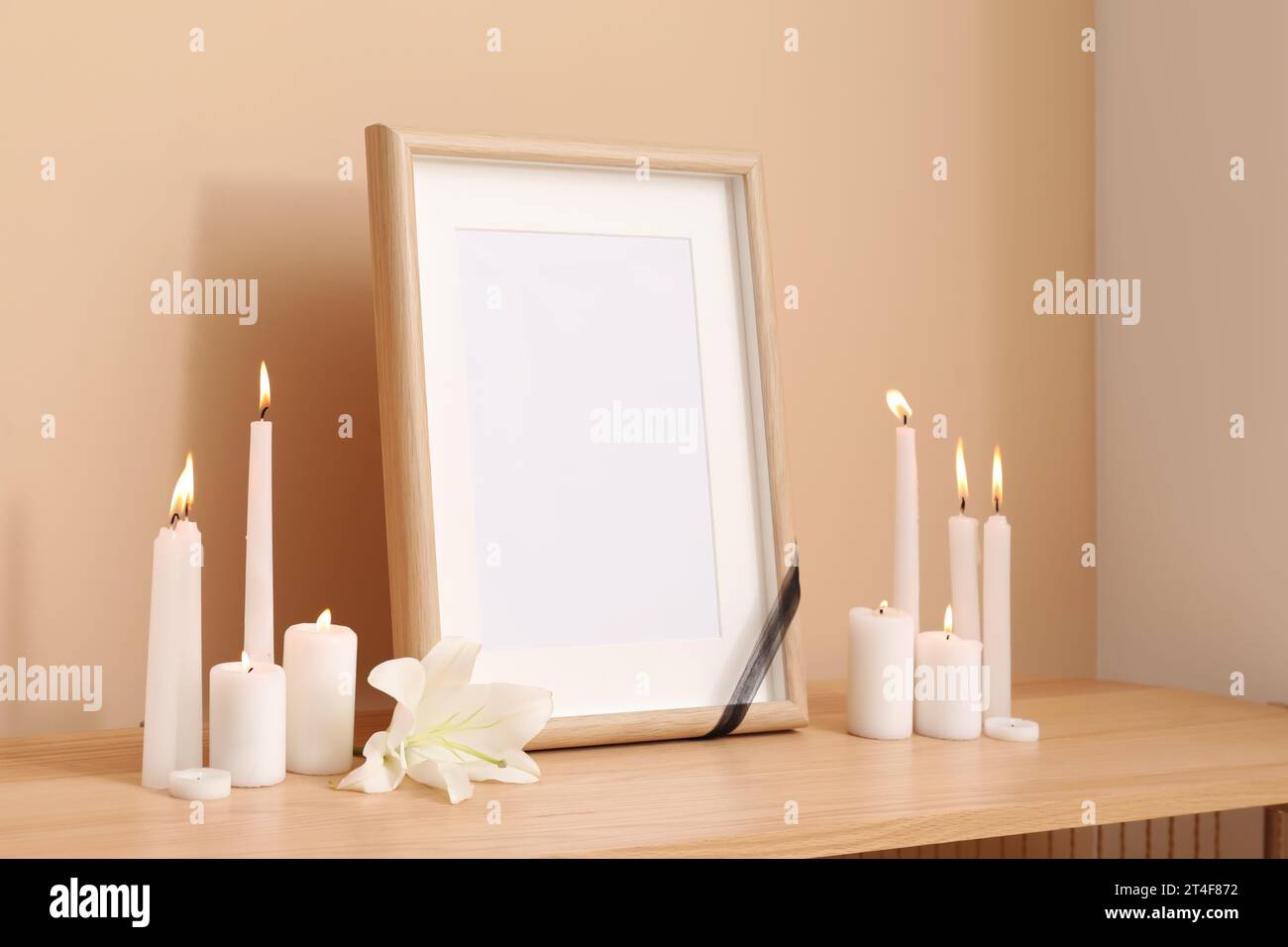 Blank mortuary frame, burning candles and lily flower on wooden table ...