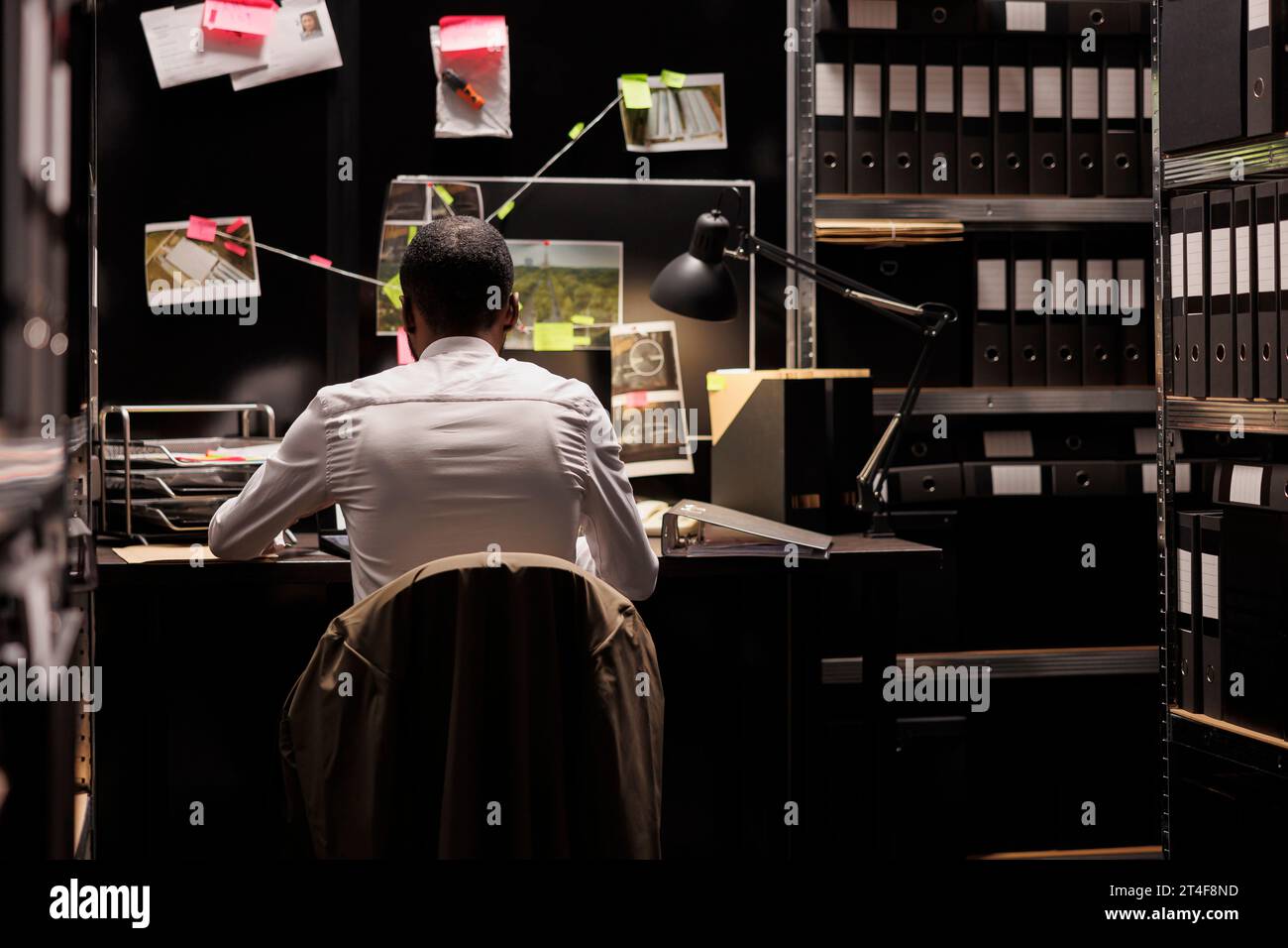 Detective sitting at desk and analyzing evidence scheme hanging on wall ...