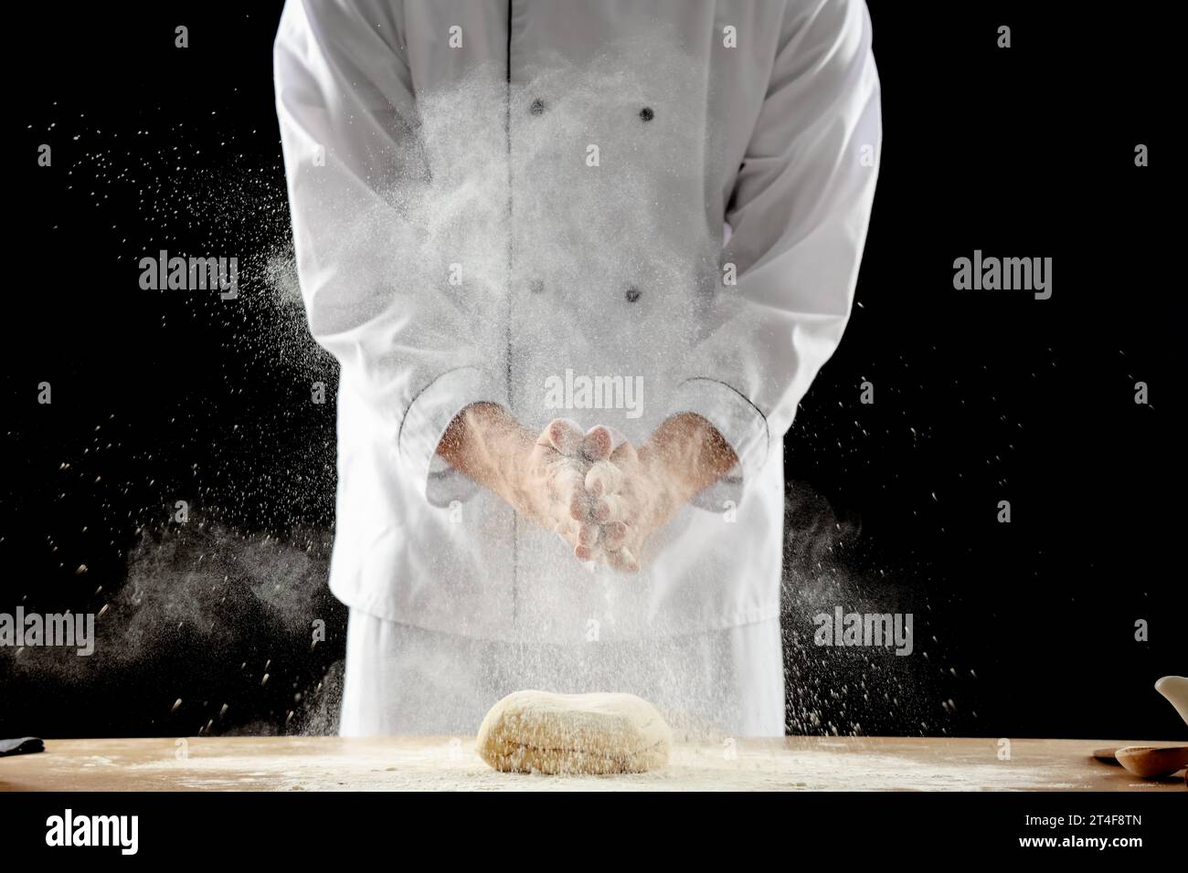 Young chef clapping and sprinkling flour over dough on table against ...