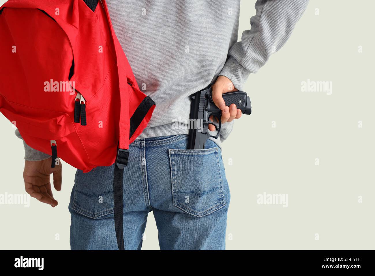 Male student with gun in pocket on light background, back view. School ...