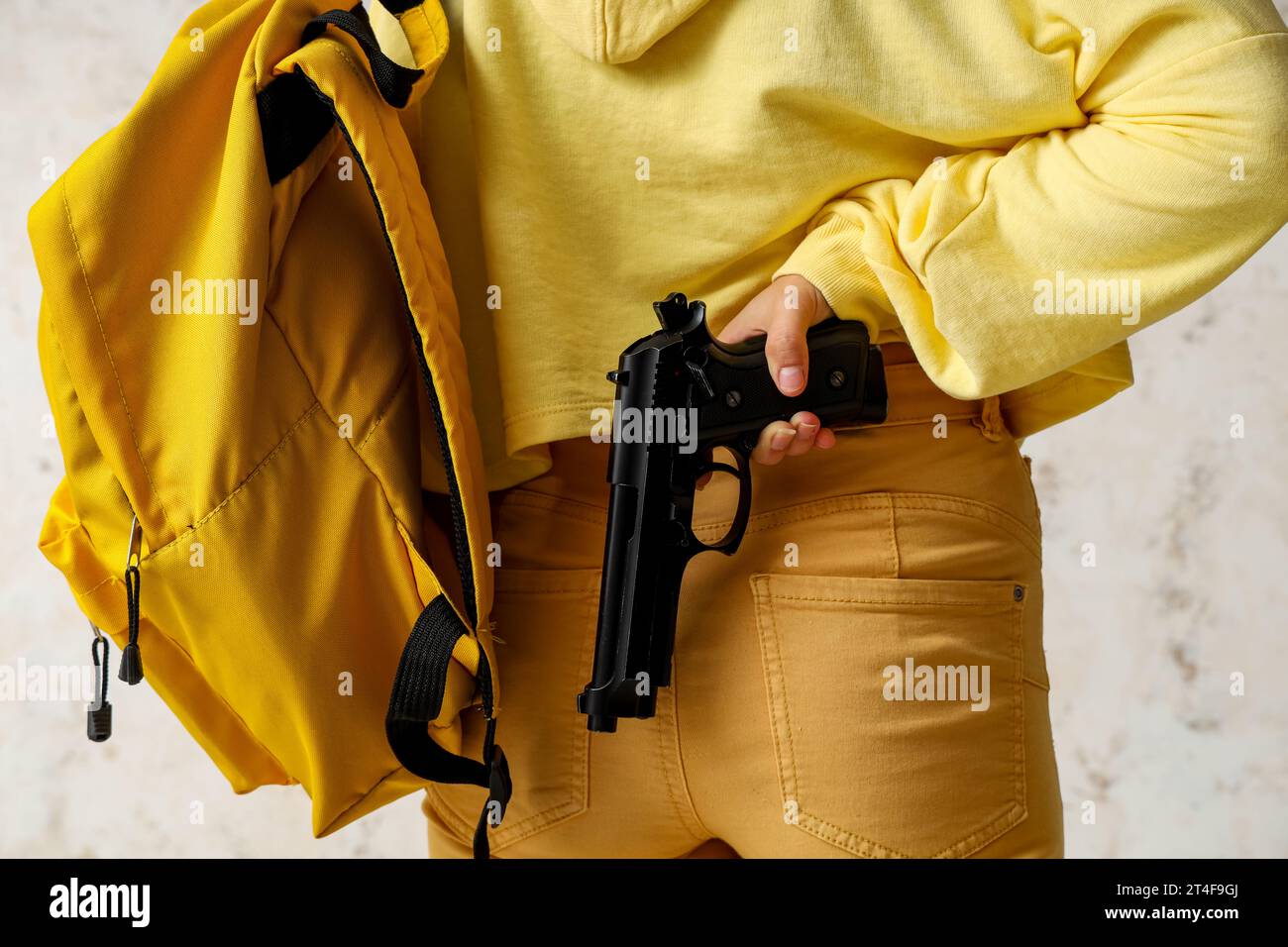 Female student with gun near grunge wall, back view. School shooting ...