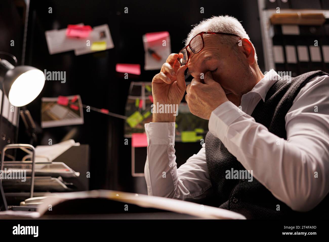 Tired elderly investigator working overtime in arhive room, analyzing ...