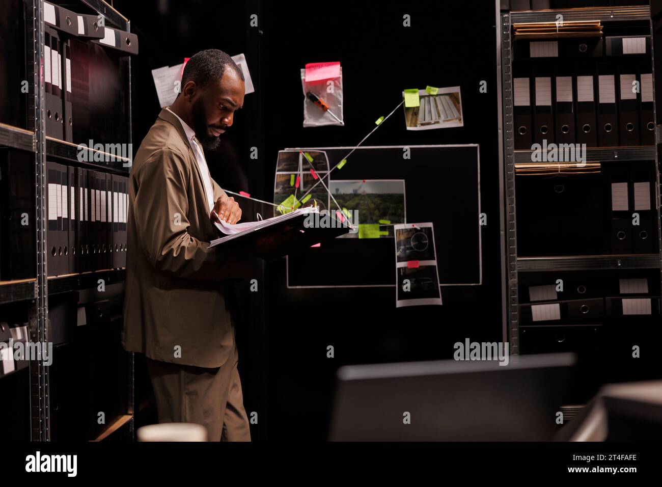 African american cop reading case file and studying detective board ...