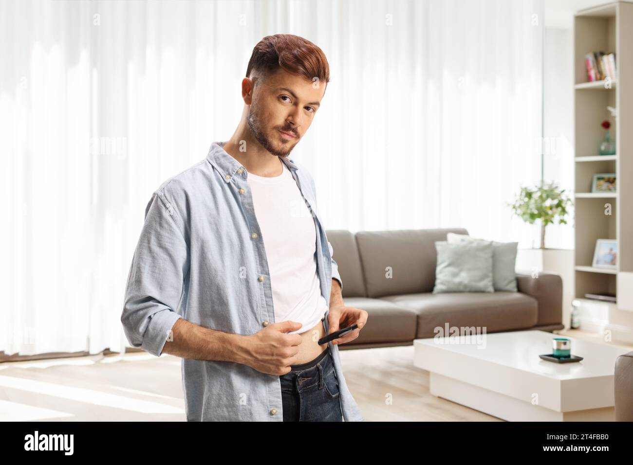 Young man injecting insulin pen in the abdomen at home in a living room ...