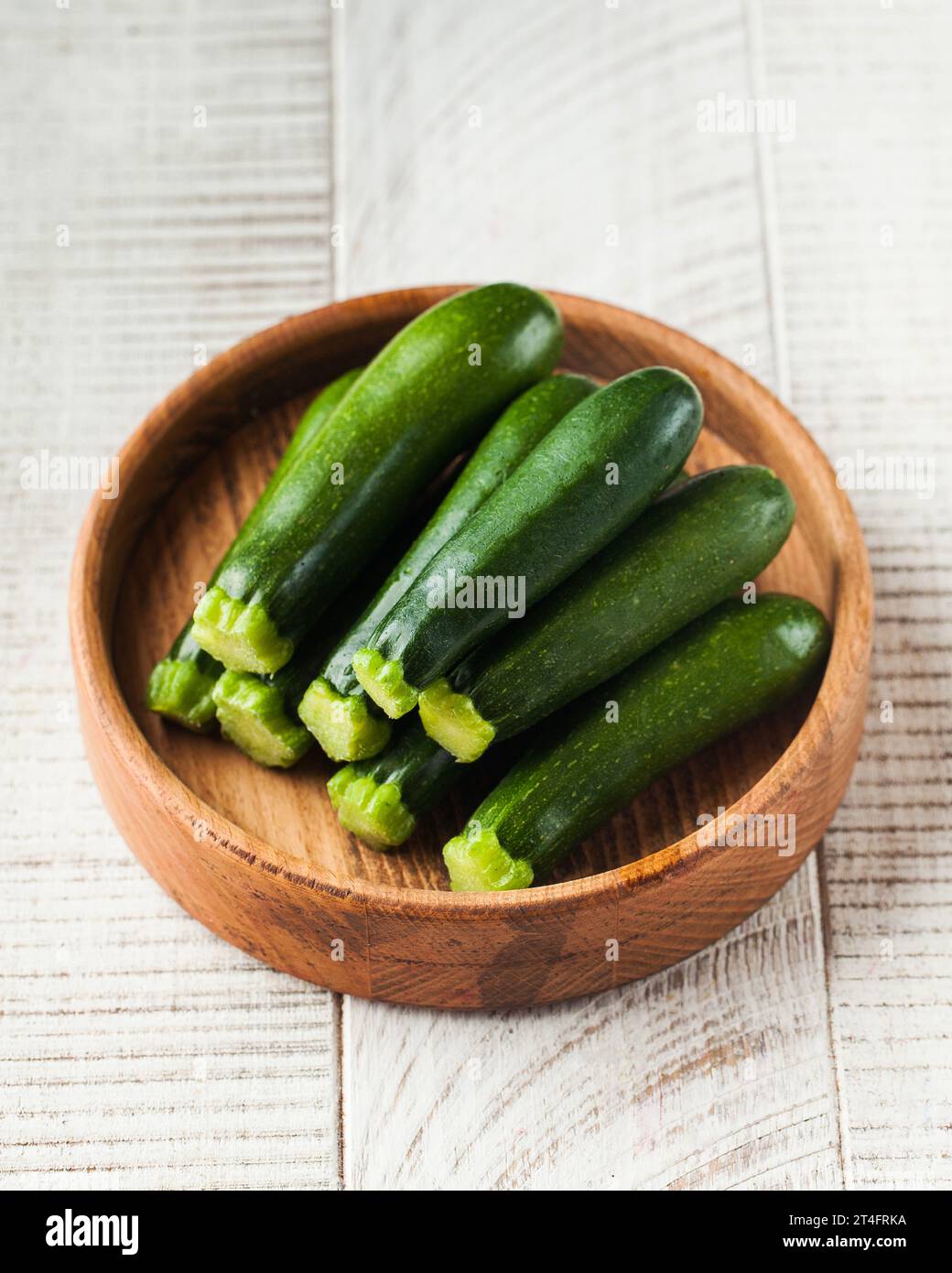 Fresh mini zucchini in a wooden plate on a white wooden background ...