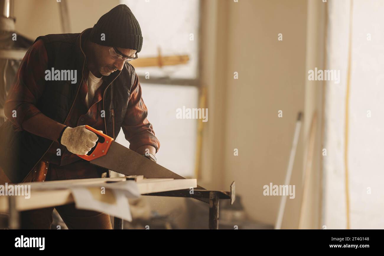 Building contractor renovating a kitchen, using a saw to cut wood. He ...