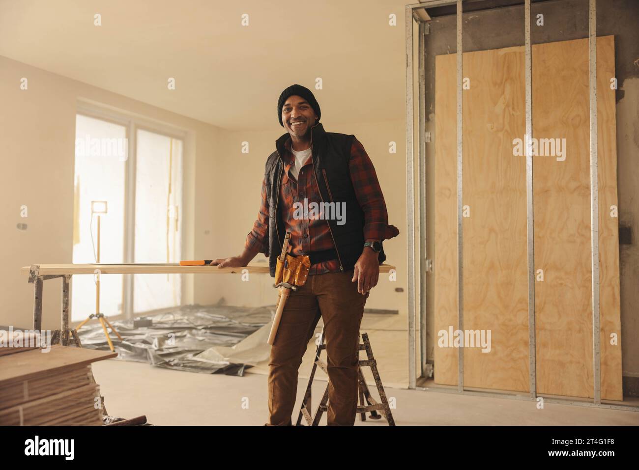 Happy contractor in a tool belt stands in a kitchen of a house under ...