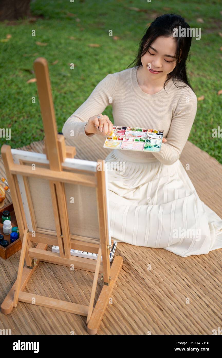 A talented and creative young Asian female artist is mixing water color ...