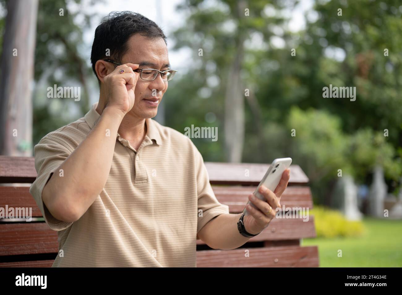 A happy retired Asian man adjusting his eyeglasses while reading ...