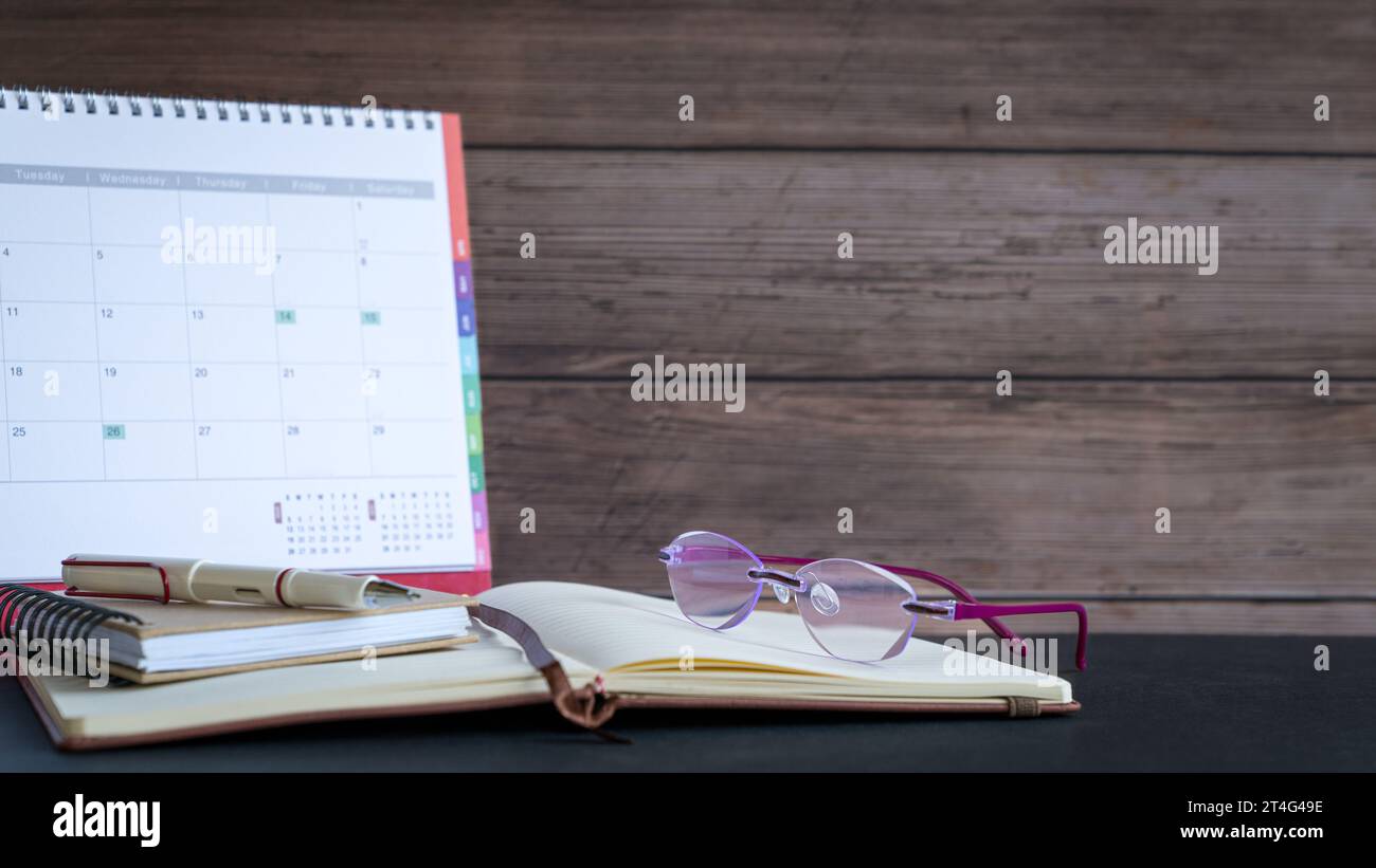 Desk standing calendar with notepads, pen and eyeglasses on desk, wood ...