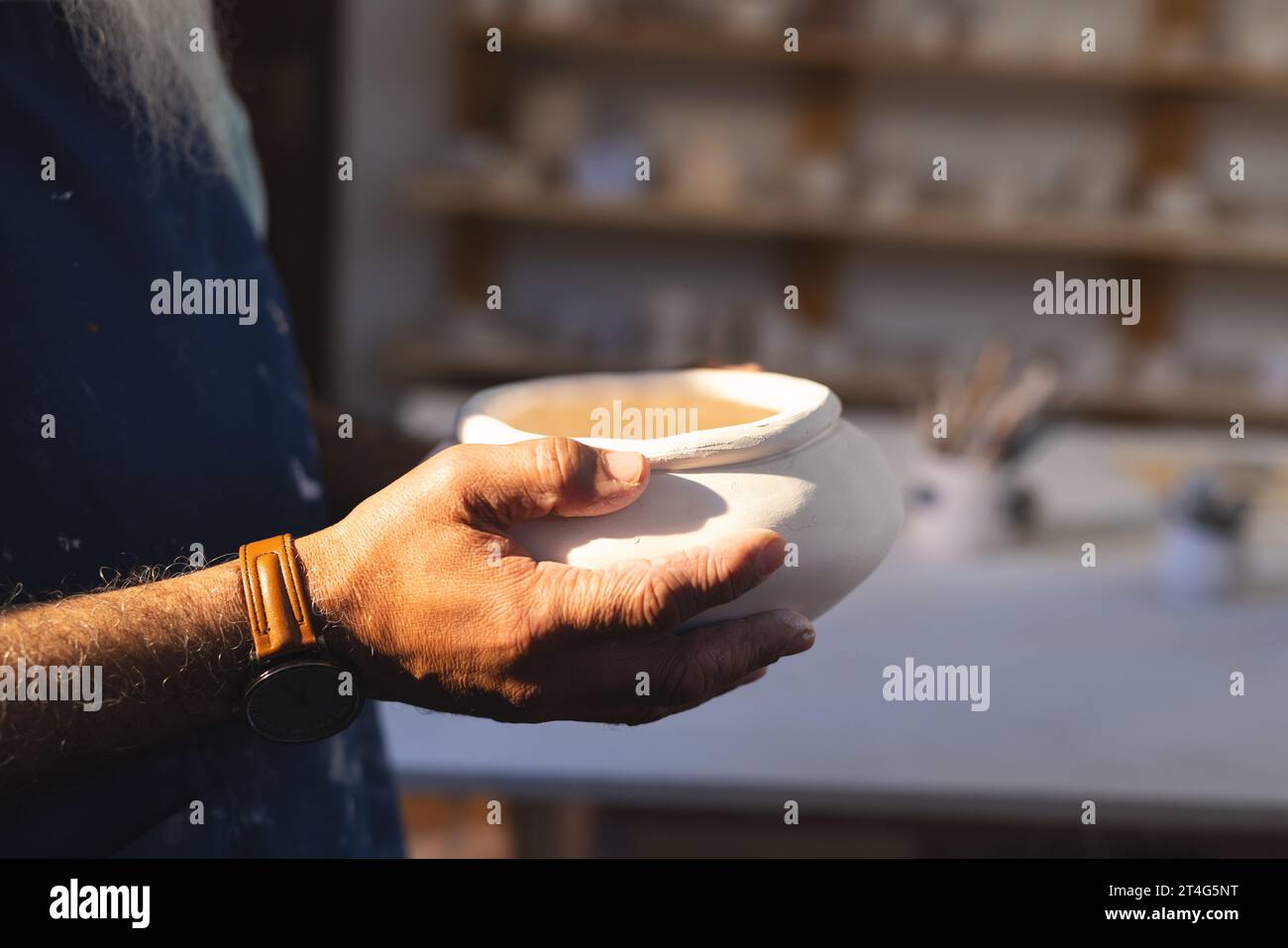 Hands of senior biracial potter holding clay vase in pottery studio ...