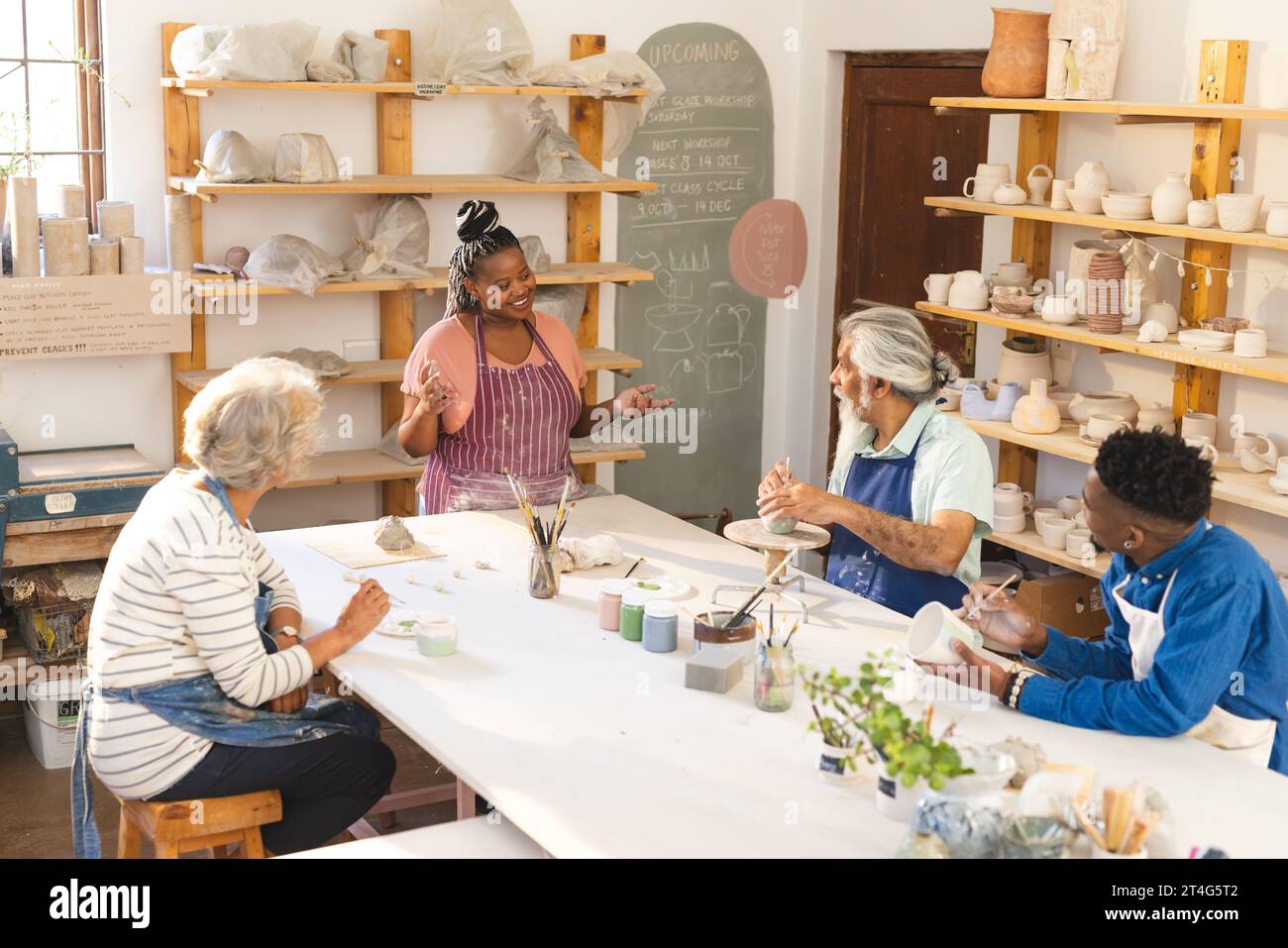 Happy diverse group of potters glazing clay jugs and discussing in ...