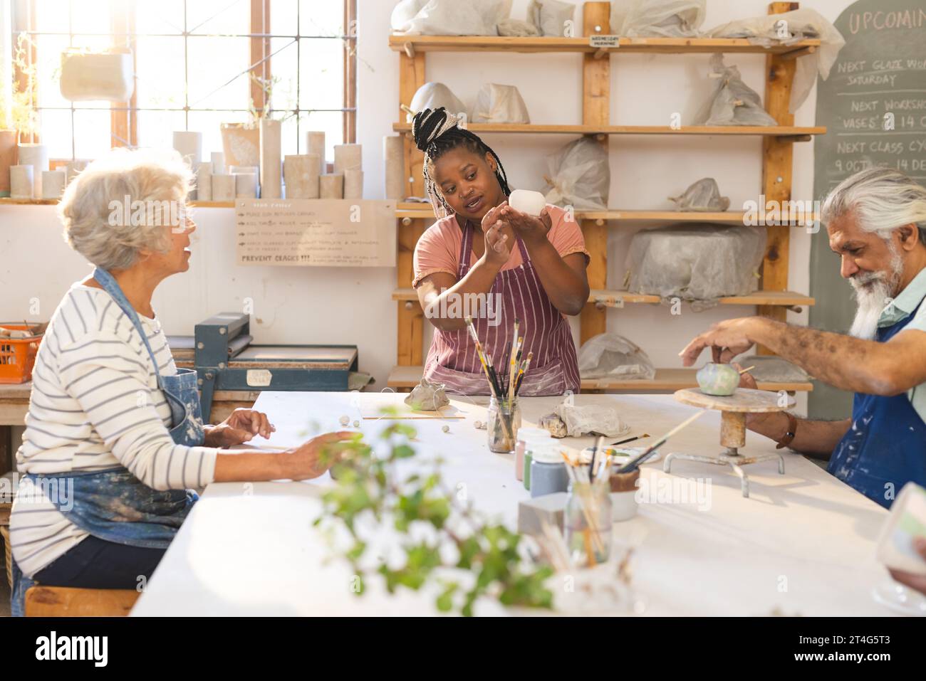 Happy diverse group of potters glazing clay jugs and discussing in ...