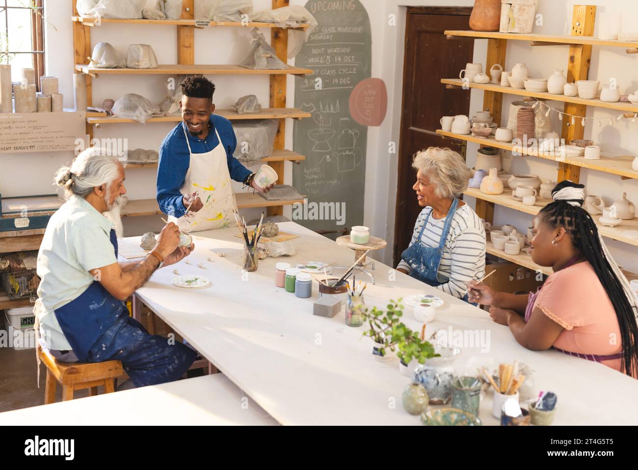 Happy diverse group of potters glazing clay jugs and discussing in ...