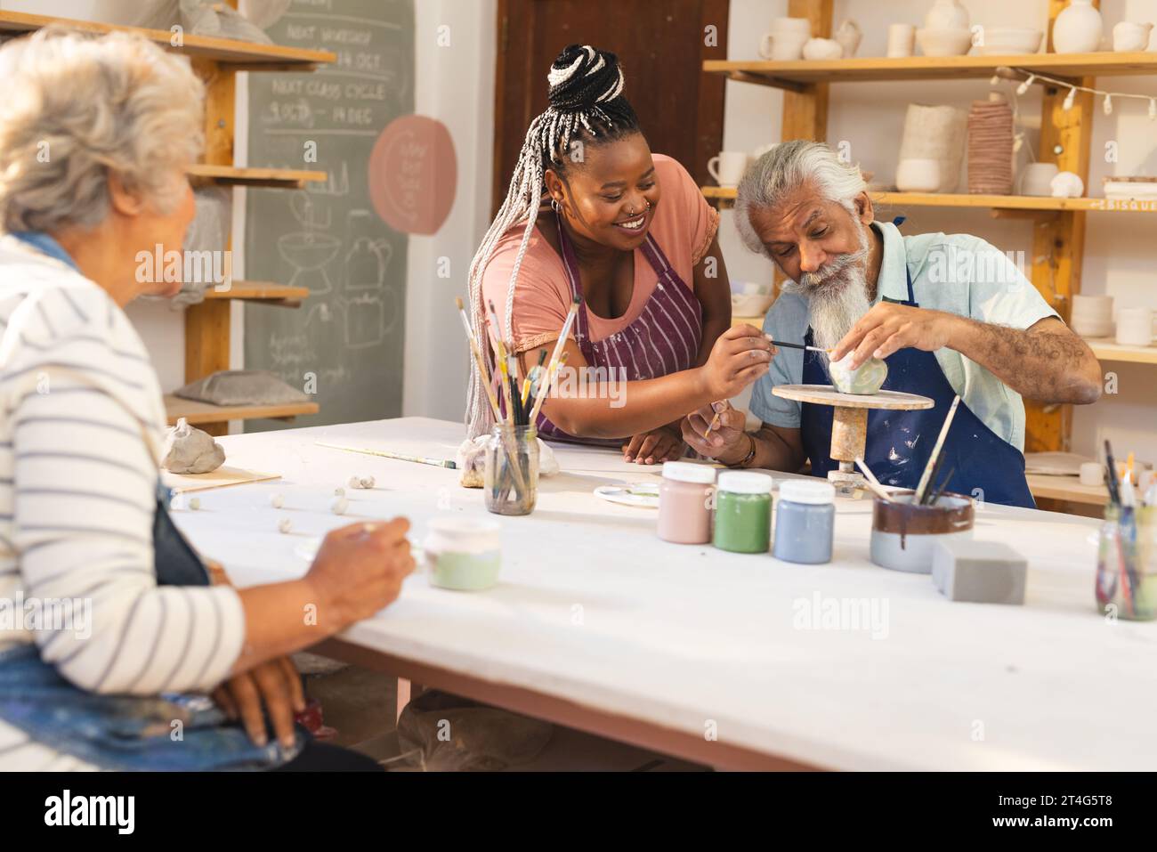 Happy diverse group of potters glazing clay jugs and smiling in pottery ...
