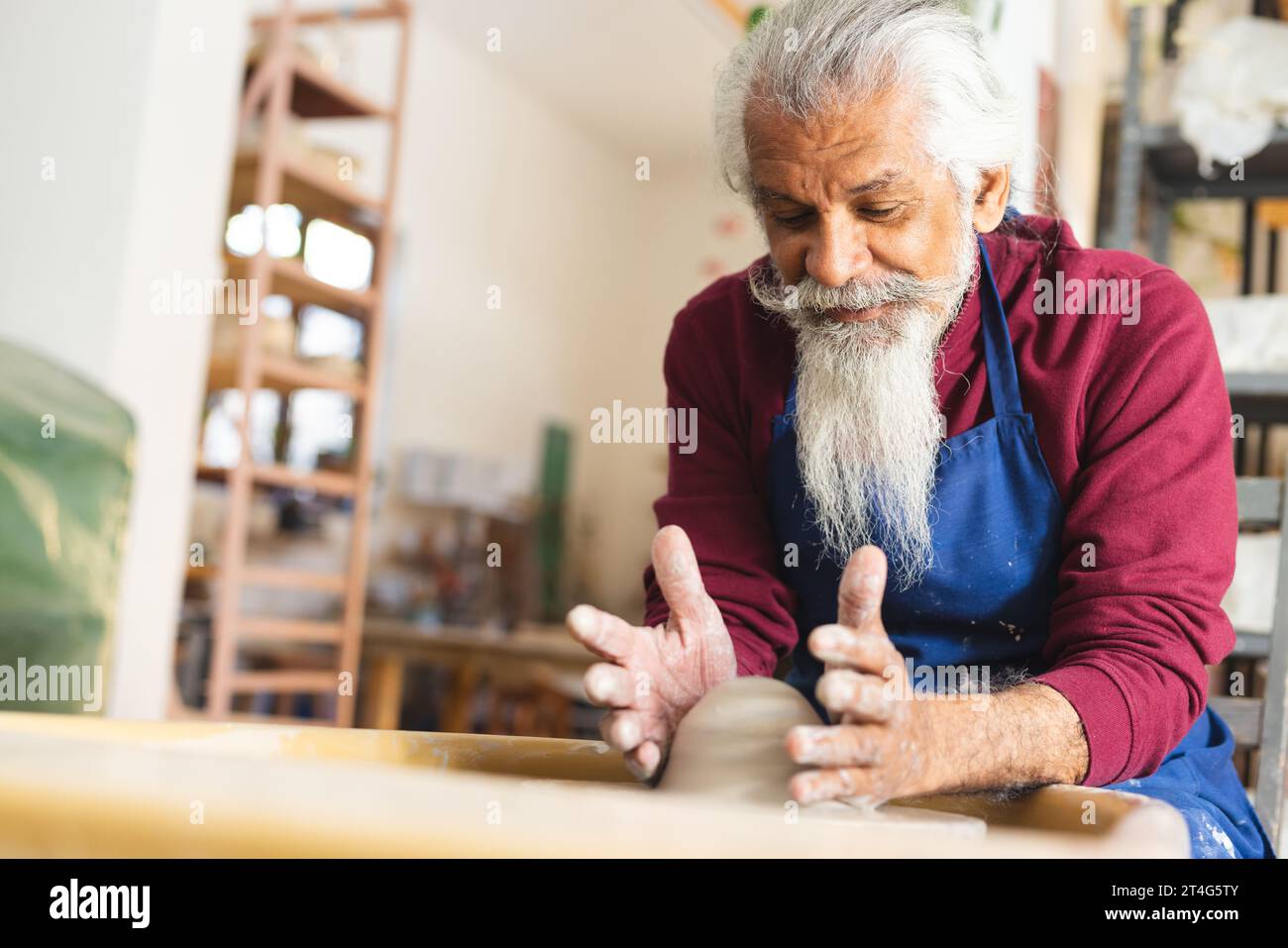 Focused biracial senior potter with long beard using potter's wheel in ...