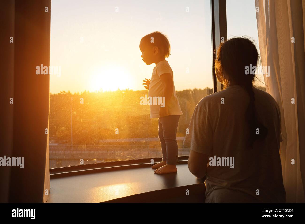 Parents with child stand in front of window in flat at sunset Stock ...