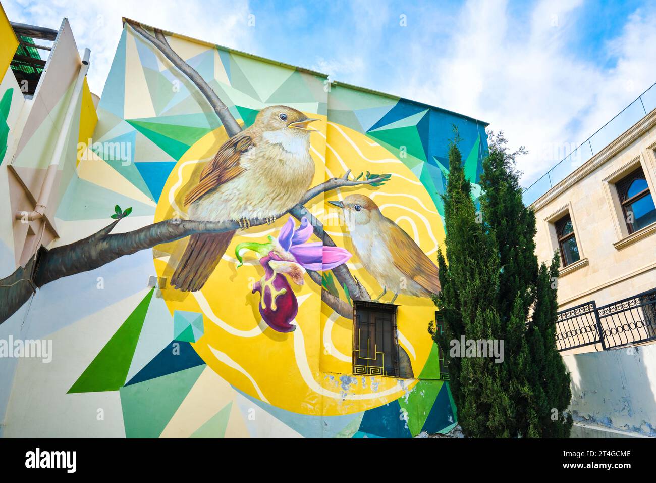 A large, wall, painted mural on a building of two birds and a blooming ...