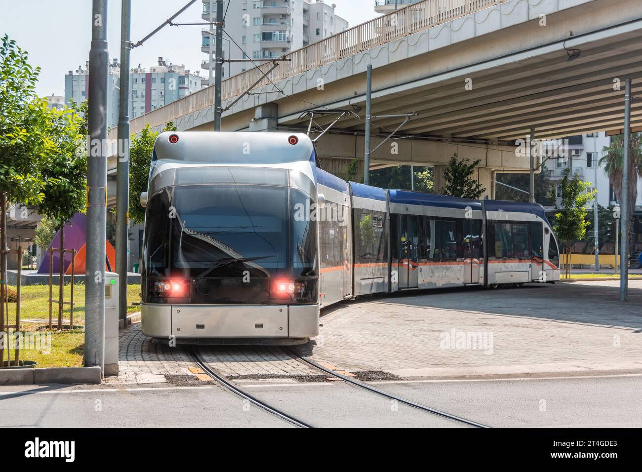 Modern comfortable tram moves along turn the streets under bridge ...
