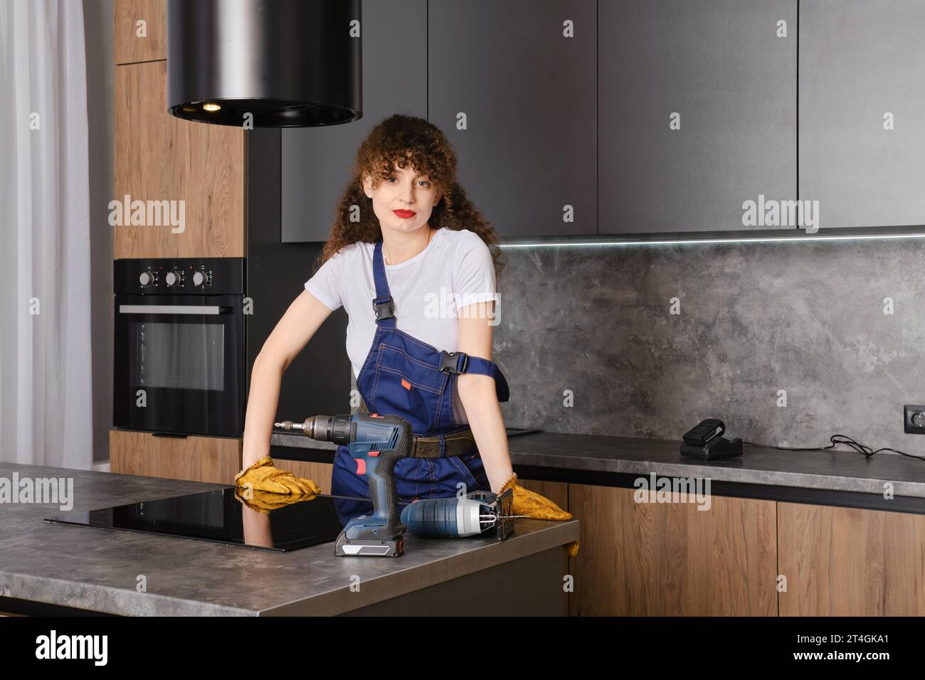 Pleased woman in overalls has finished assembling kitchen furniture ...