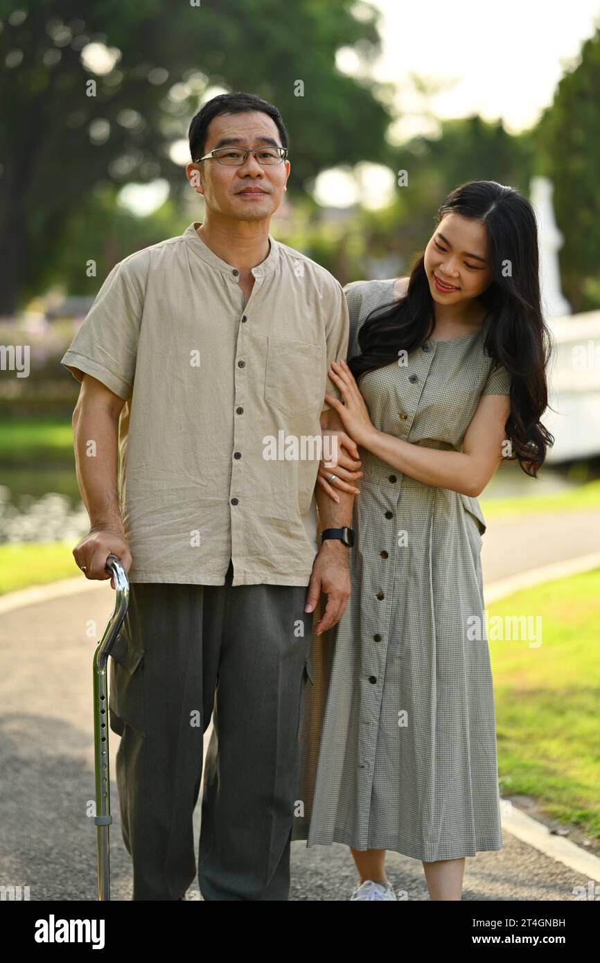 Caring young adult daughter walking with middle age father at park ...
