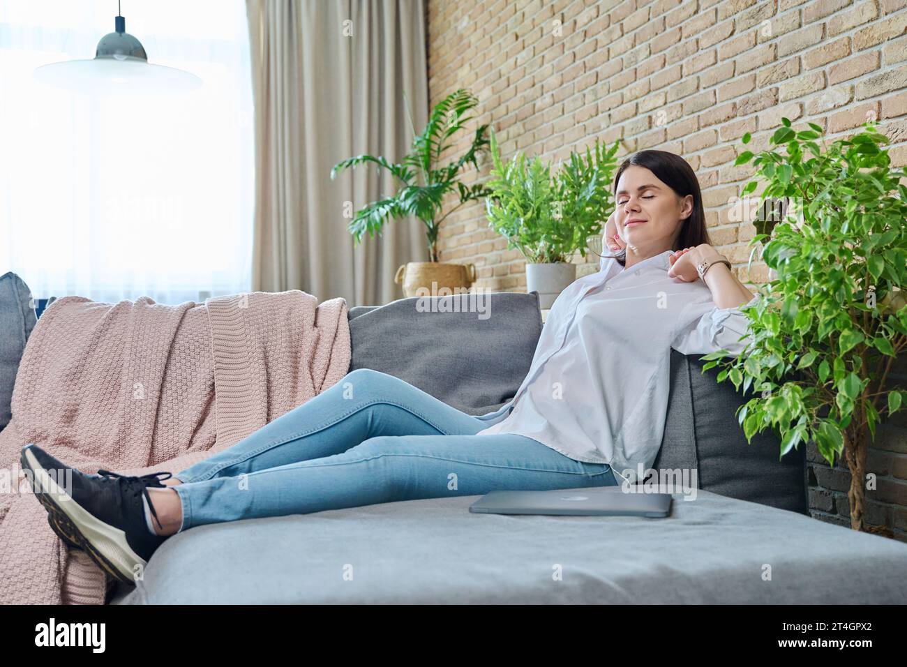 Relaxed young woman with raised arms sitting on sofa in living room ...