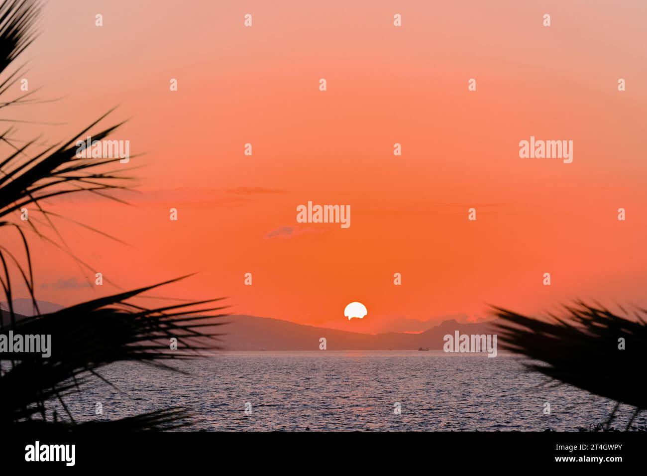 Crimson sky and full sphere sun at sunset by the sea behind the hills ...