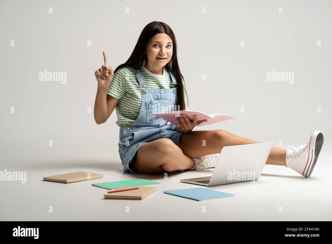 Clever schoolgirl sitting on floor, studying, pointing finger with ...