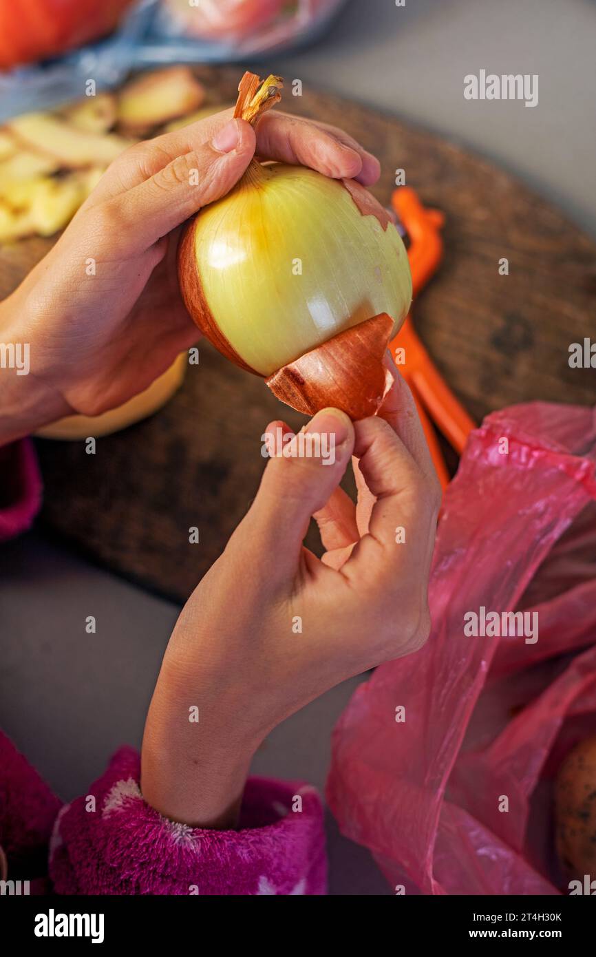 children's hands hold an onion and peel the skin in the kitchen before ...