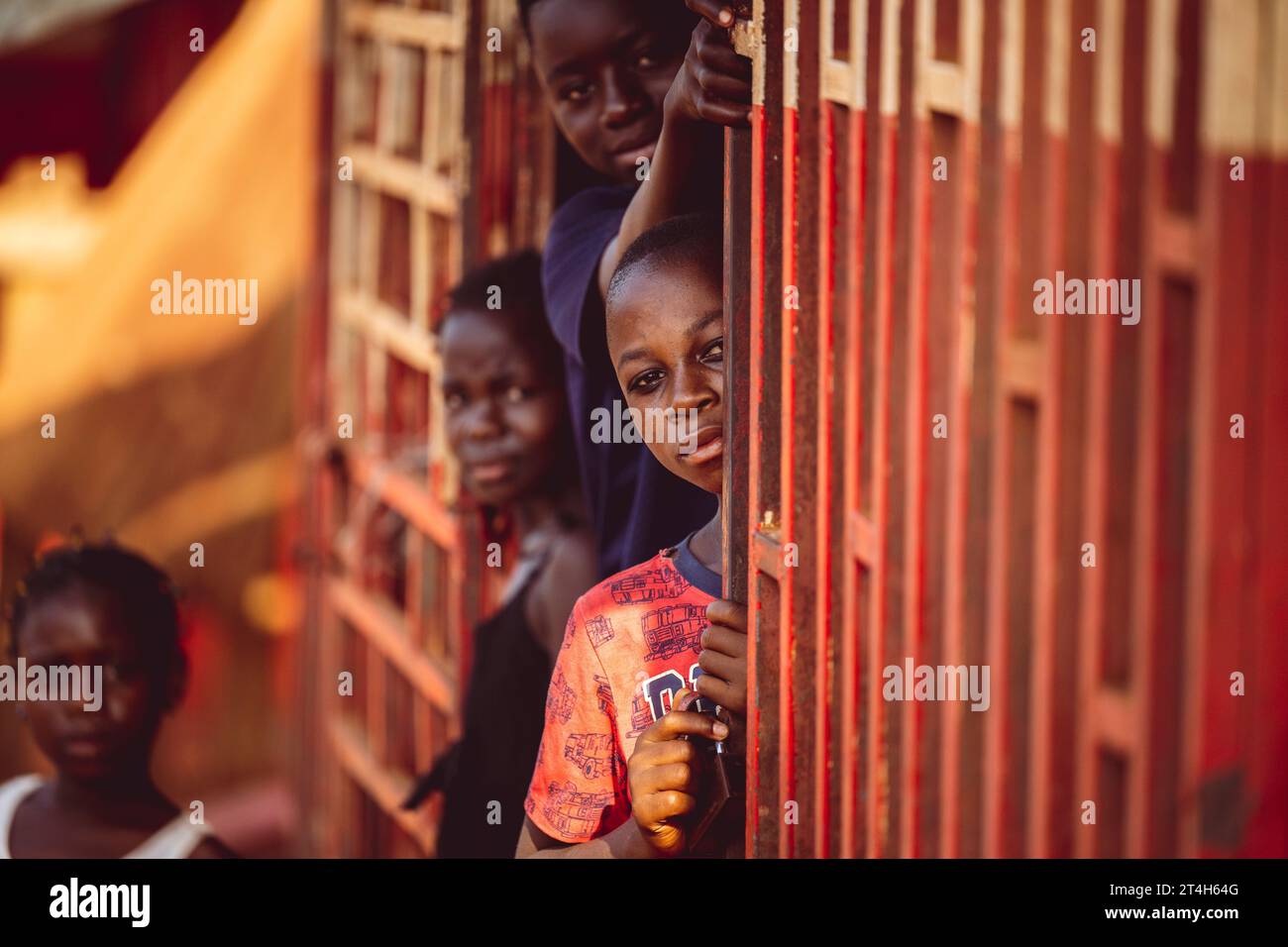 A group of African people looking out from behind a bright orange door ...