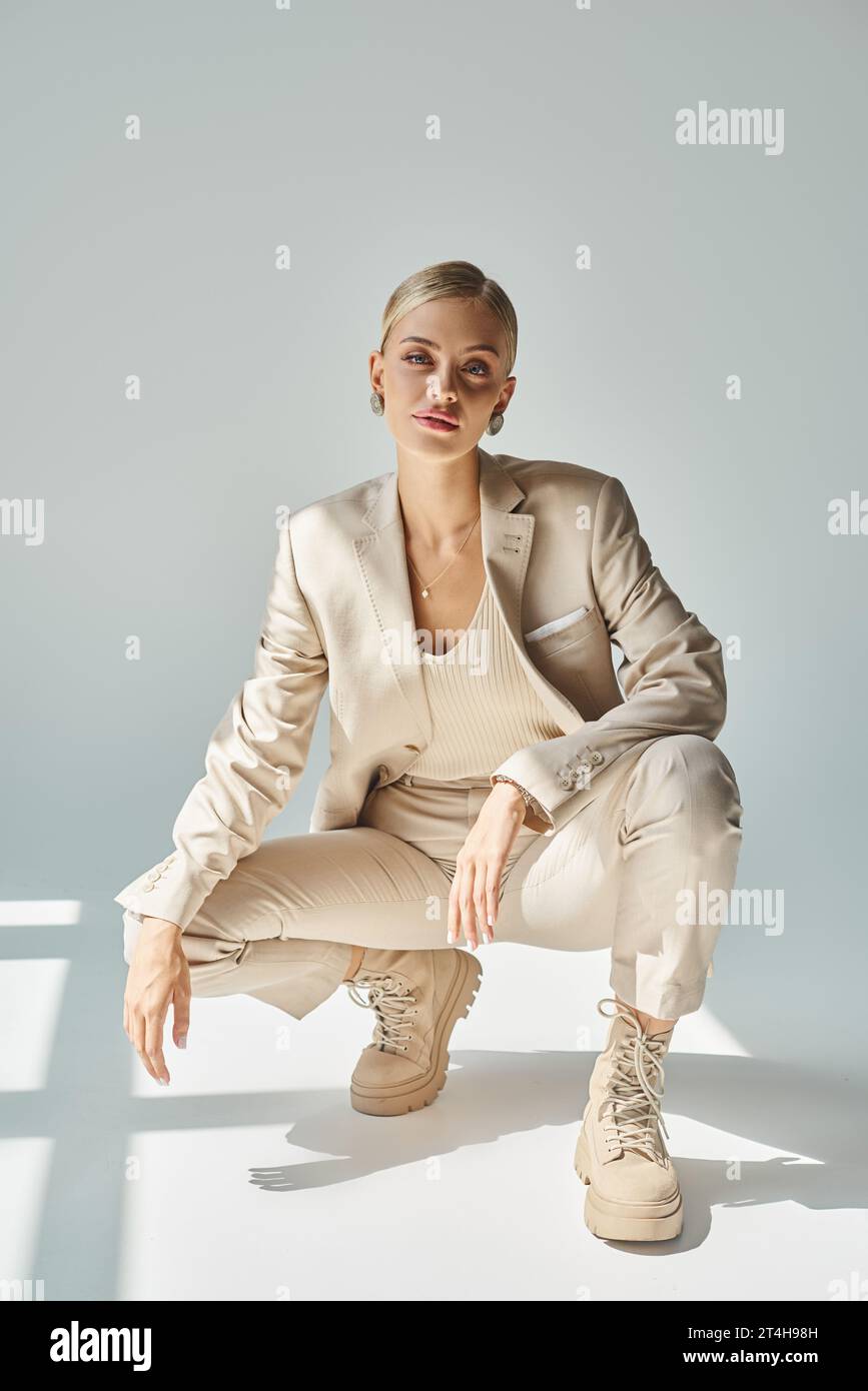 trendy blonde woman in beige suit and laced boots posing on haunches on ...