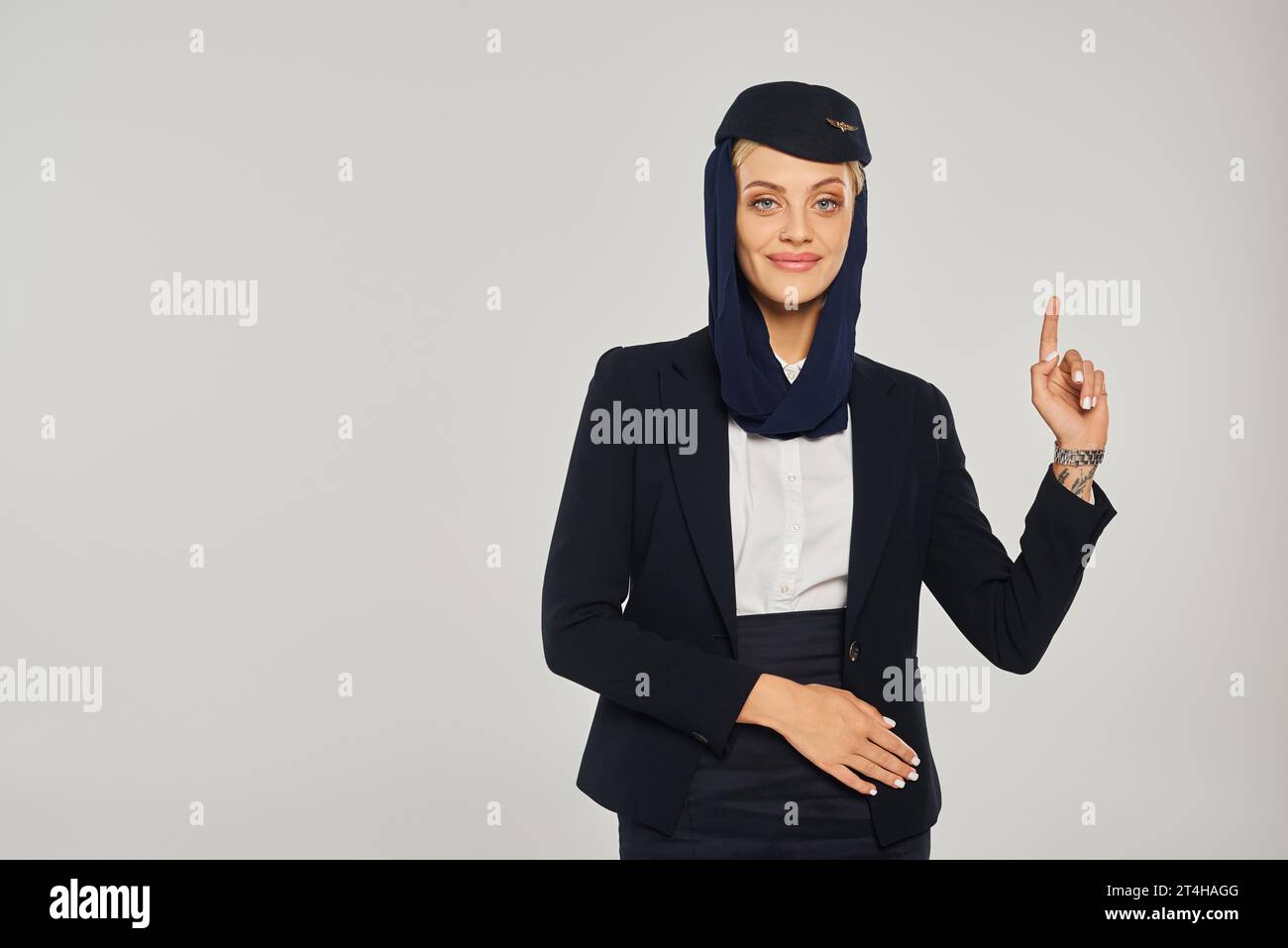 cheerful air hostess in dress code of arabian airlines pointing up with ...