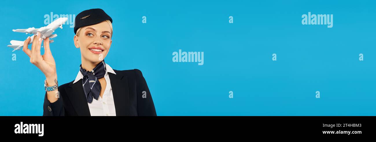 happy and charming air hostess in stylish uniform holding airplane ...