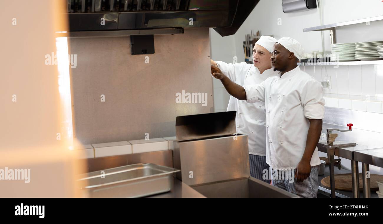 Diverse male chefs operating appliance in commercial kitchen at cooking ...