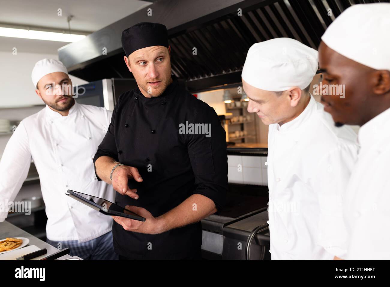 Multiracial male chef head explaining over digital tablet to students ...