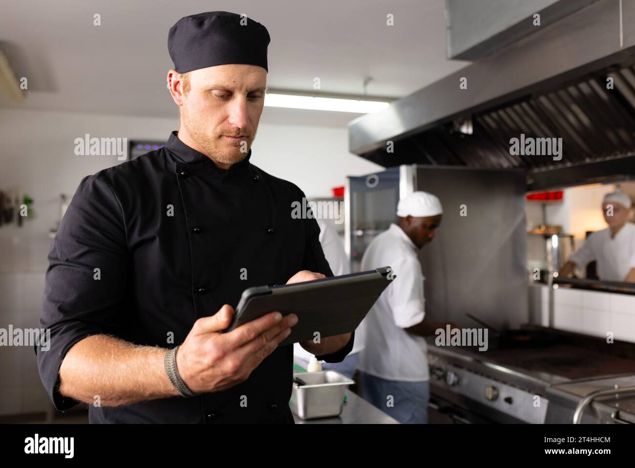 Diverse male chef teacher working over tablet while student cooking ...