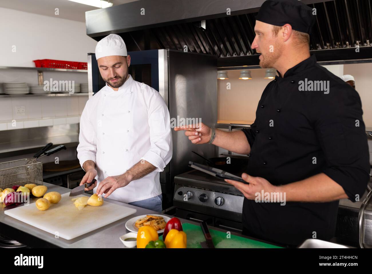 Caucasian male chef teacher guiding student in cutting potatoes in ...
