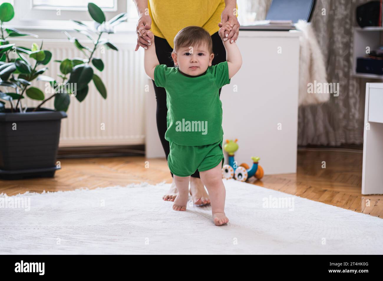 Caring mother teaching little son to walk on white rug holding hands ...