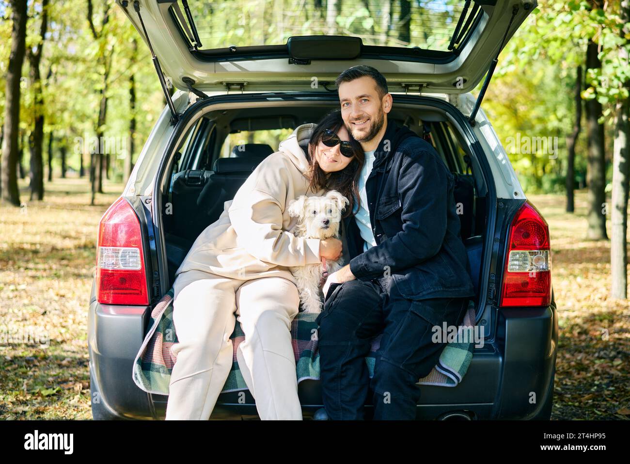 Loving couple embracing hugging with their white dog in the hatchback ...