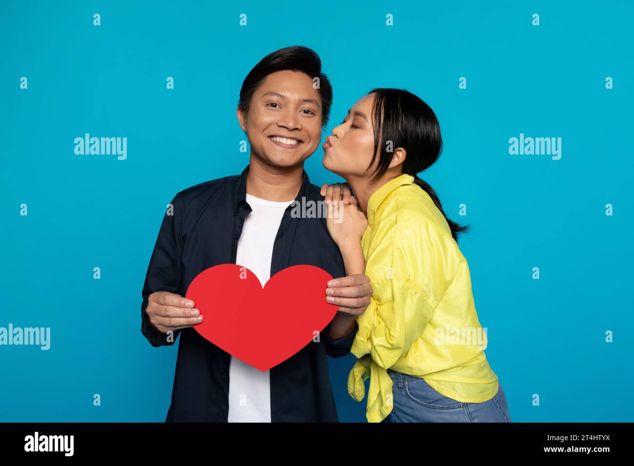 Cheerful millennial japanese wife in casual kiss husband, hold red ...