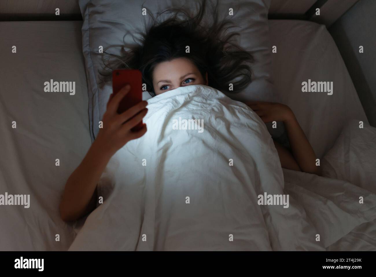 Sleepy female watching her smartphone in bed at night. Dependence on ...