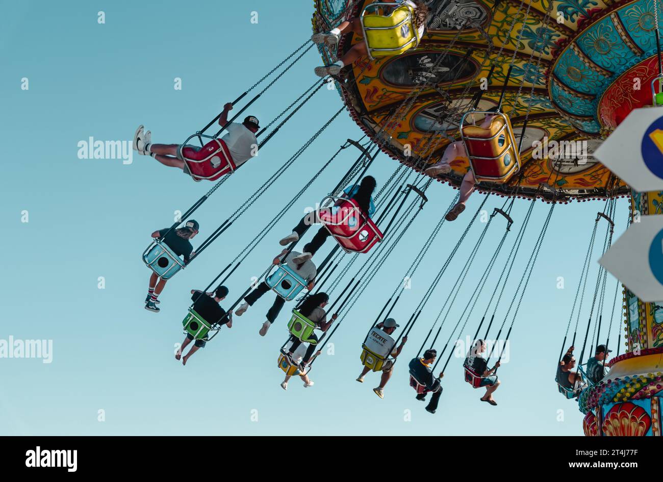People riding the Sea Swings at Santa Cruz Boardwalk against a blue sky ...
