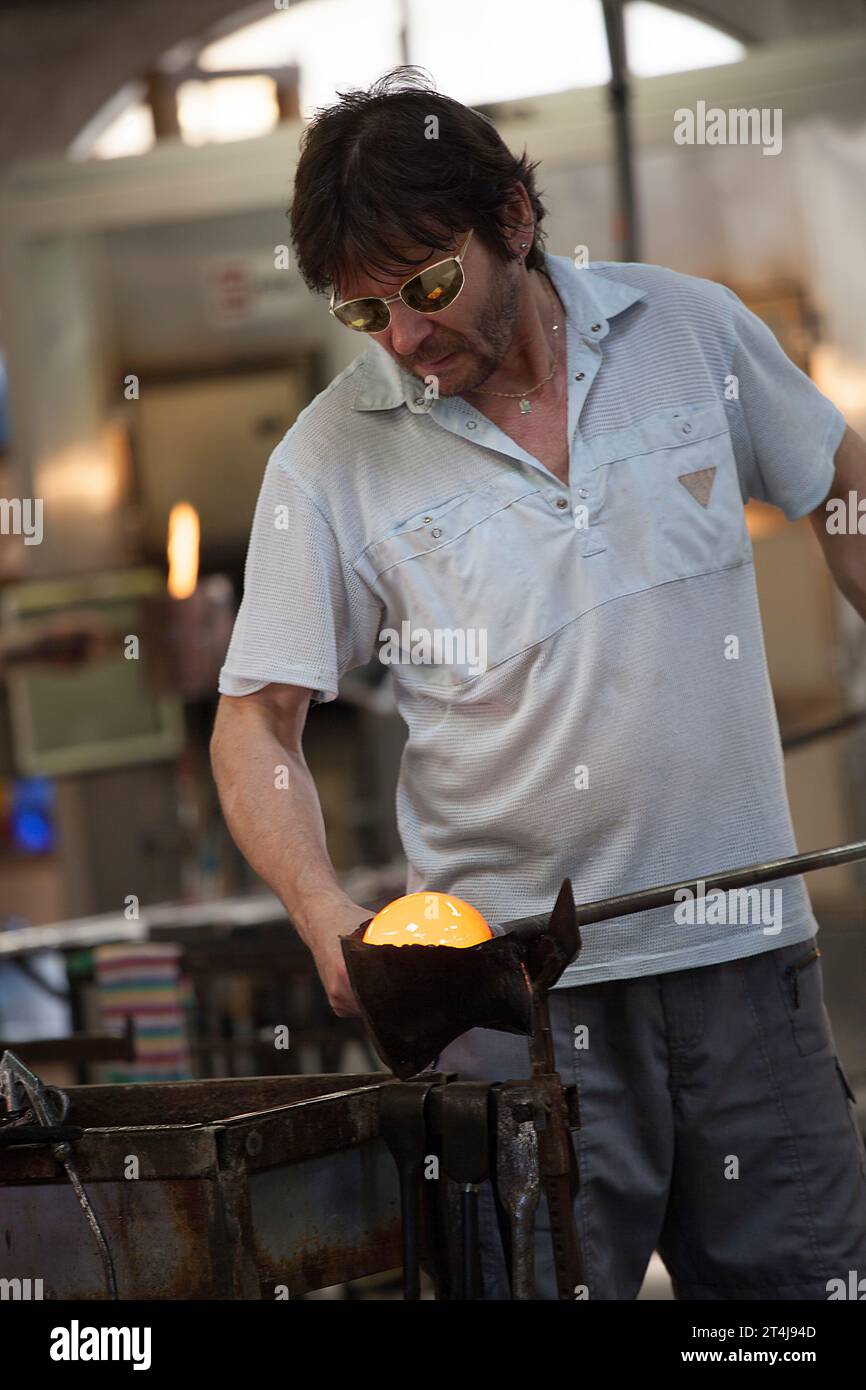 A sculptor molds a unique piece of glass inside a glass blowing factory ...