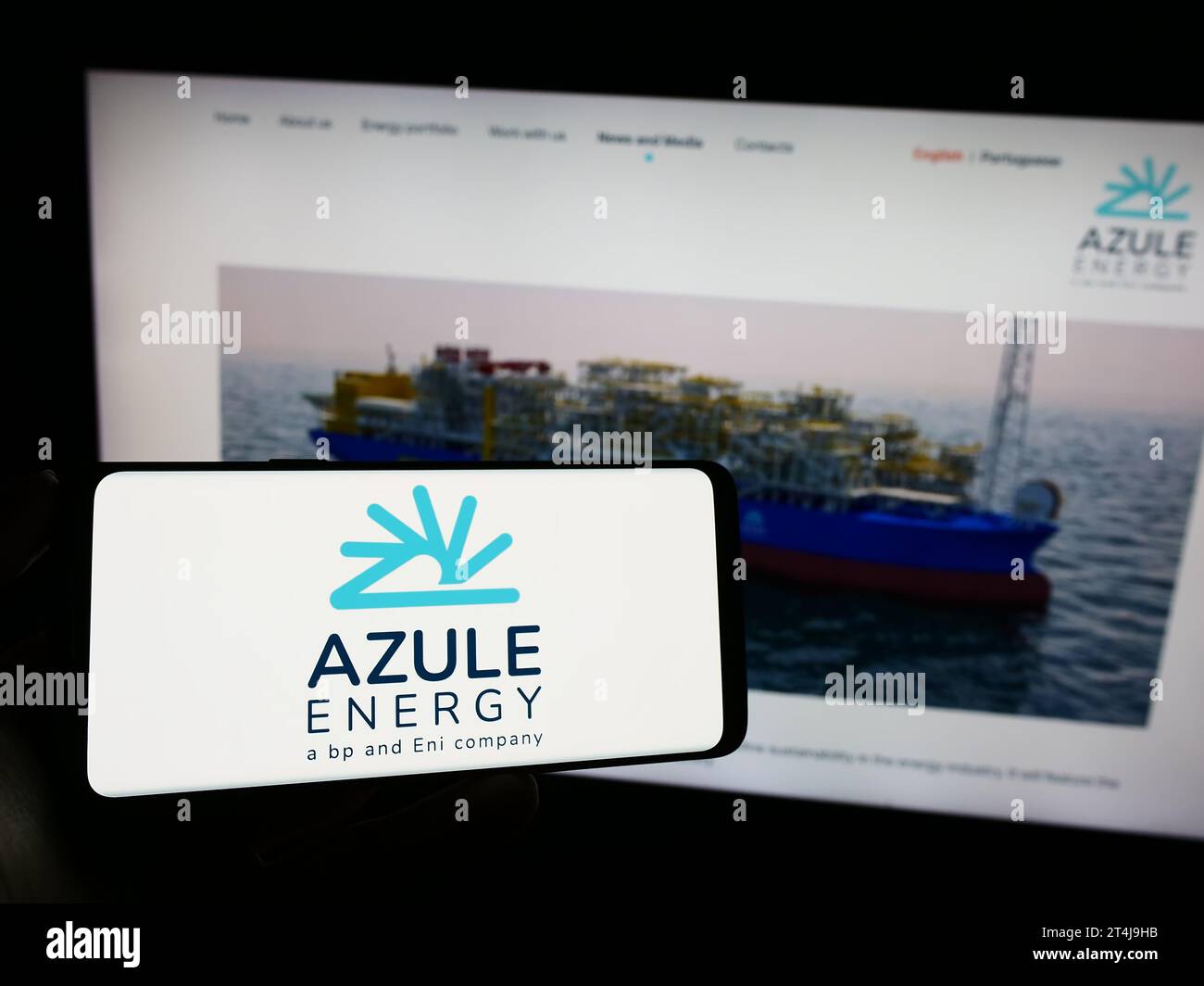 Person holding mobile phone with logo of Angolan oil company Azule Energy in front of business ...