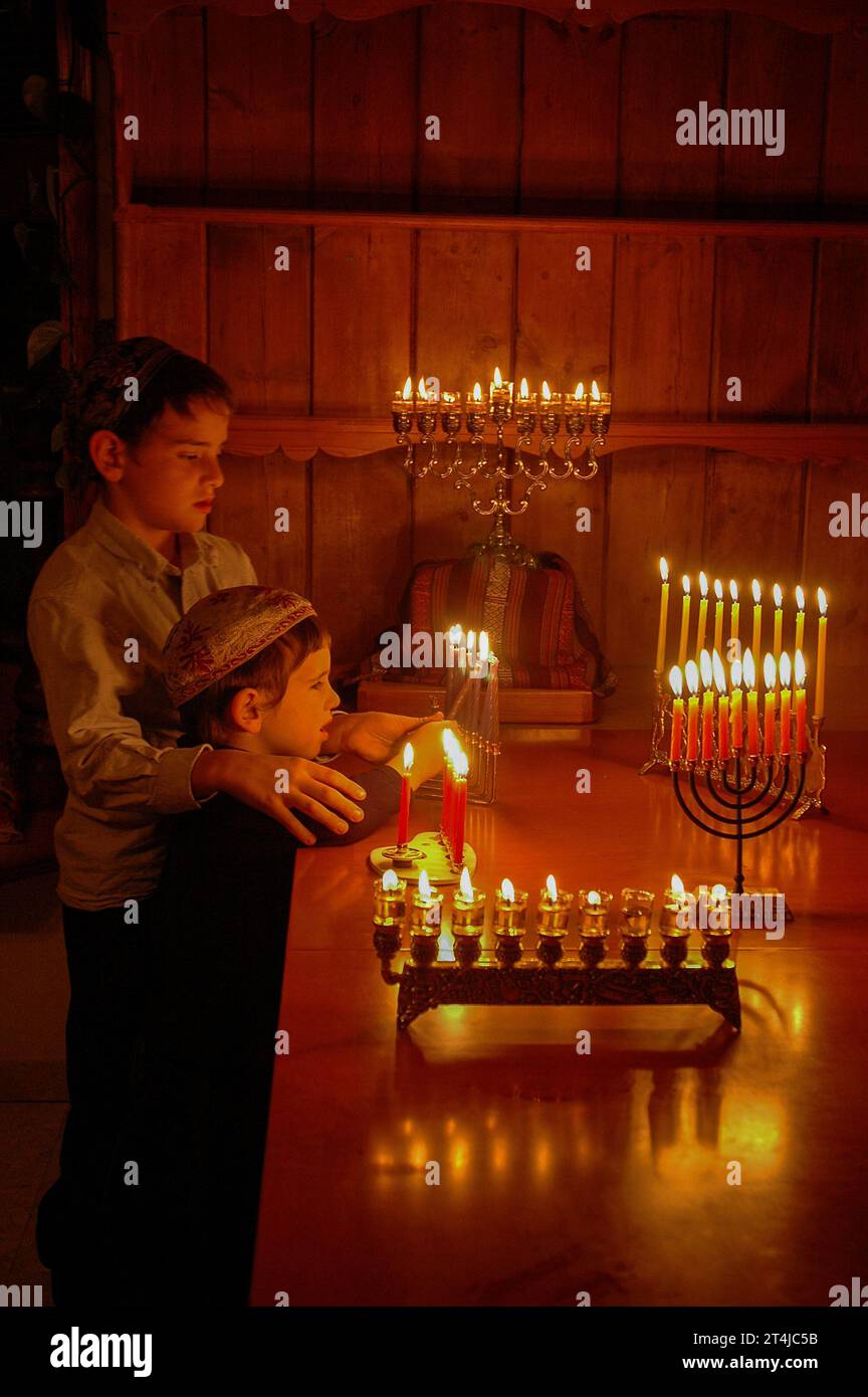 Two young boys hold a burning candle and light the Hanukkah menorah ...